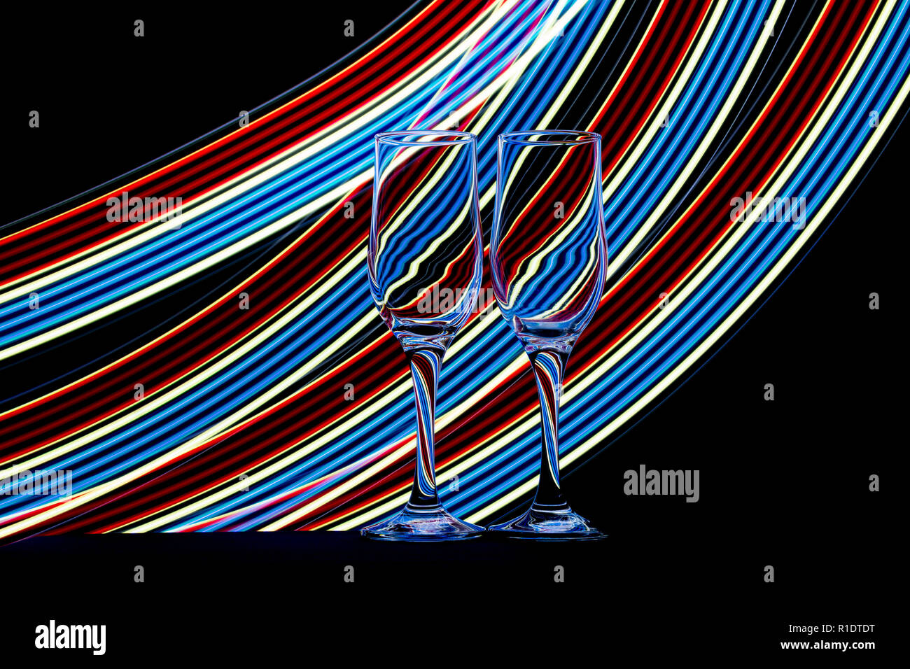 Two champagne glasses with streaks of multicoloured neon light behind ...