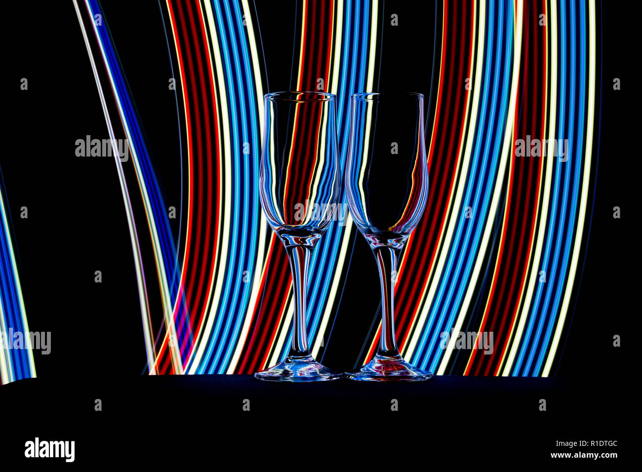 Two champagne glasses with streaks of multicoloured neon light behind ...