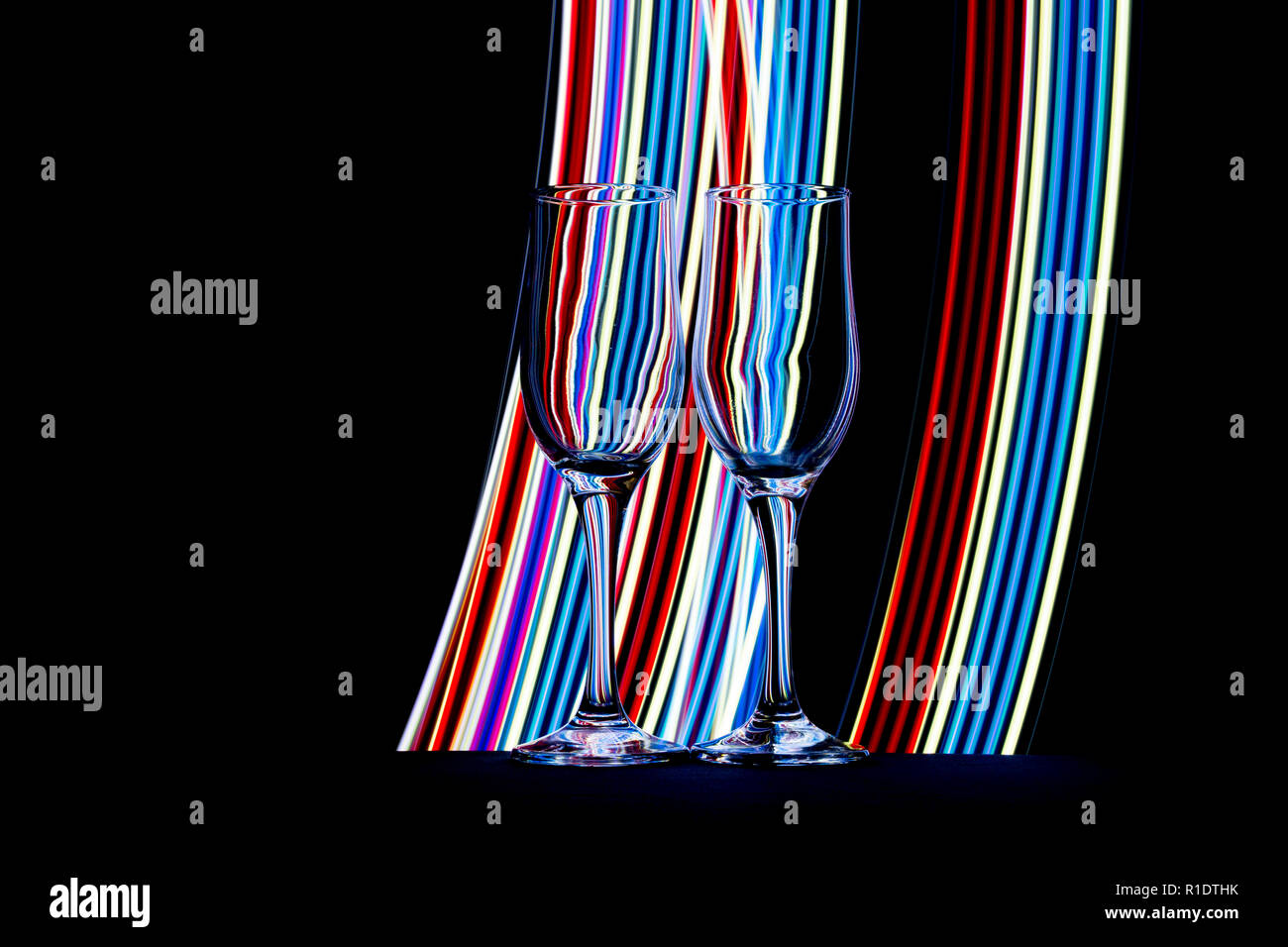 Two champagne glasses with streaks of multicoloured neon light behind ...
