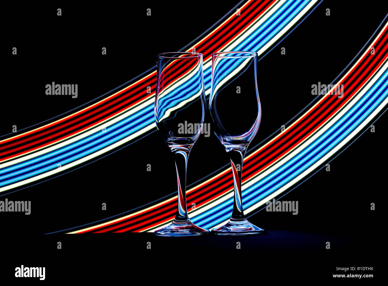 Two champagne glasses with streaks of multicoloured neon light behind ...
