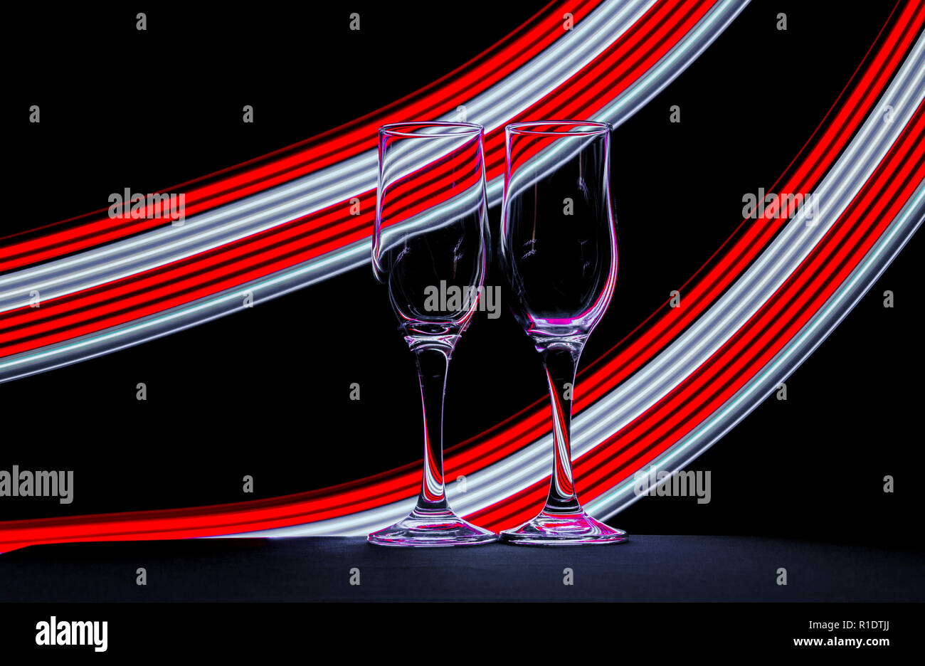 Two champagne glasses with streaks of multicoloured neon light behind ...
