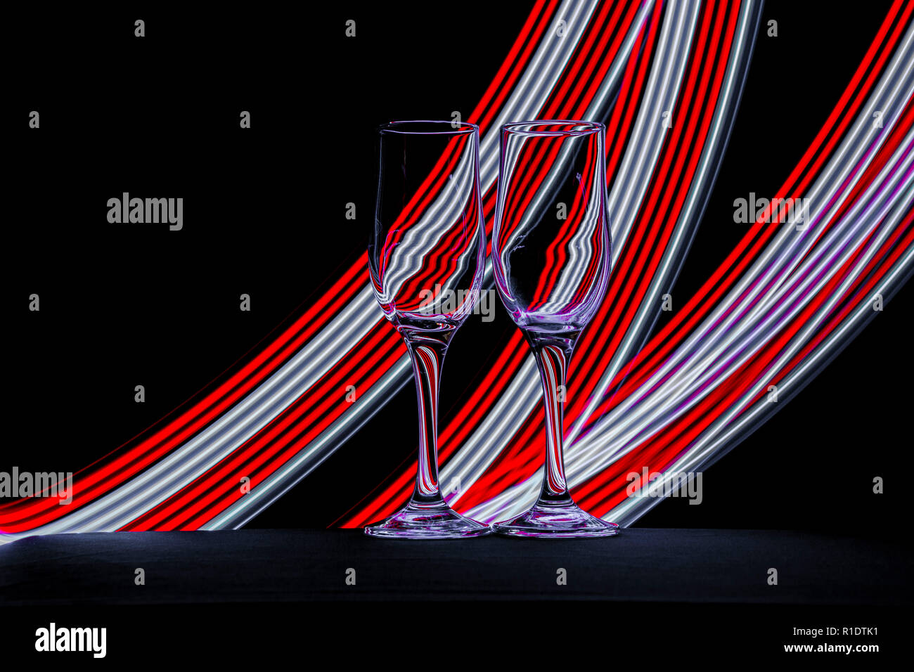 Two champagne glasses with streaks of multicoloured neon light behind ...