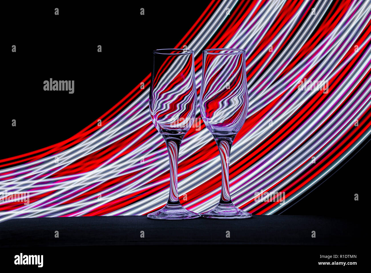 Two champagne glasses with streaks of multicoloured neon light behind ...