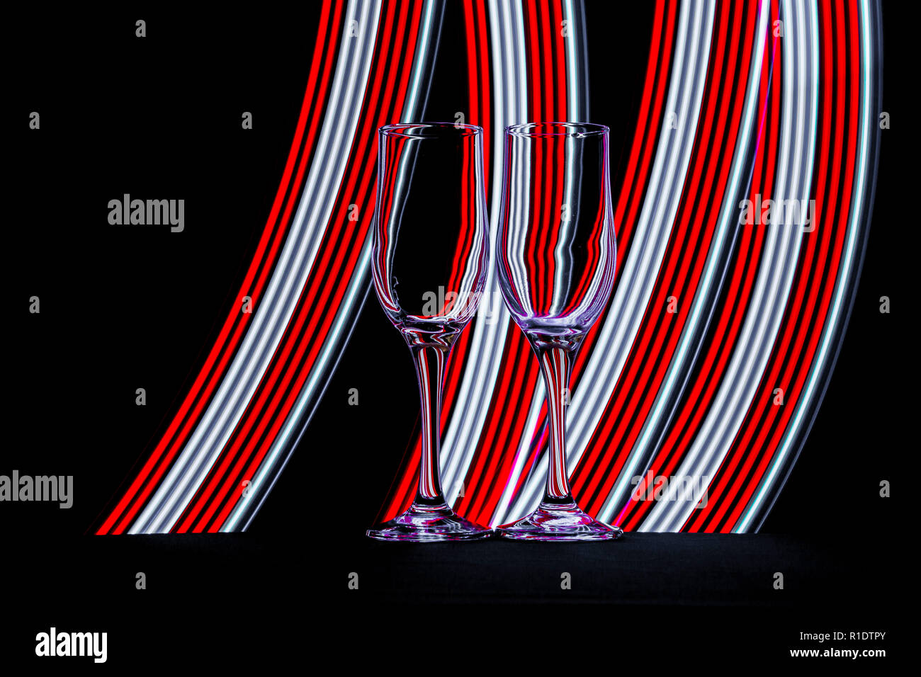 Two champagne glasses with streaks of multicoloured neon light behind ...