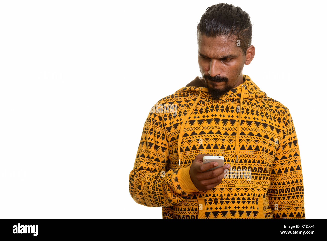 Young Indian man holding mobile phone while thinking studio portrait ...