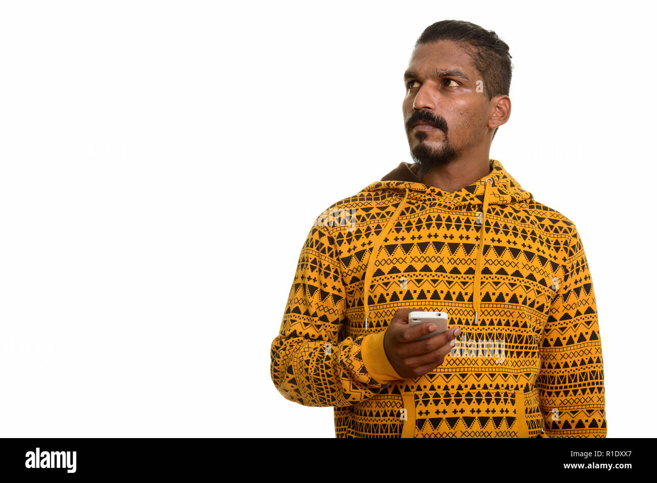 Young Indian man holding mobile phone while thinking Stock Photo - Alamy