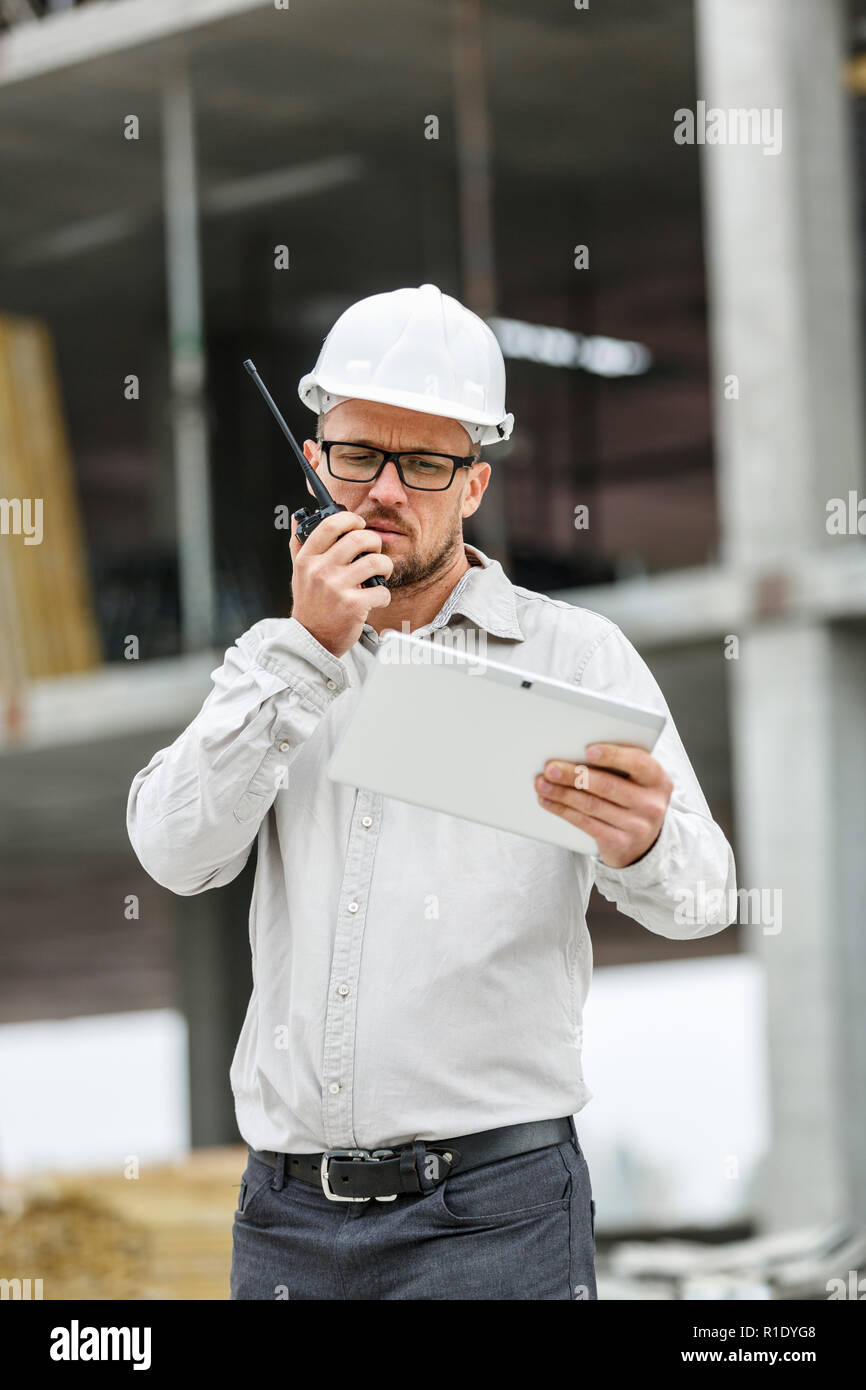 Male head engineer wearing white safety hardhat with walkie talkie and ...