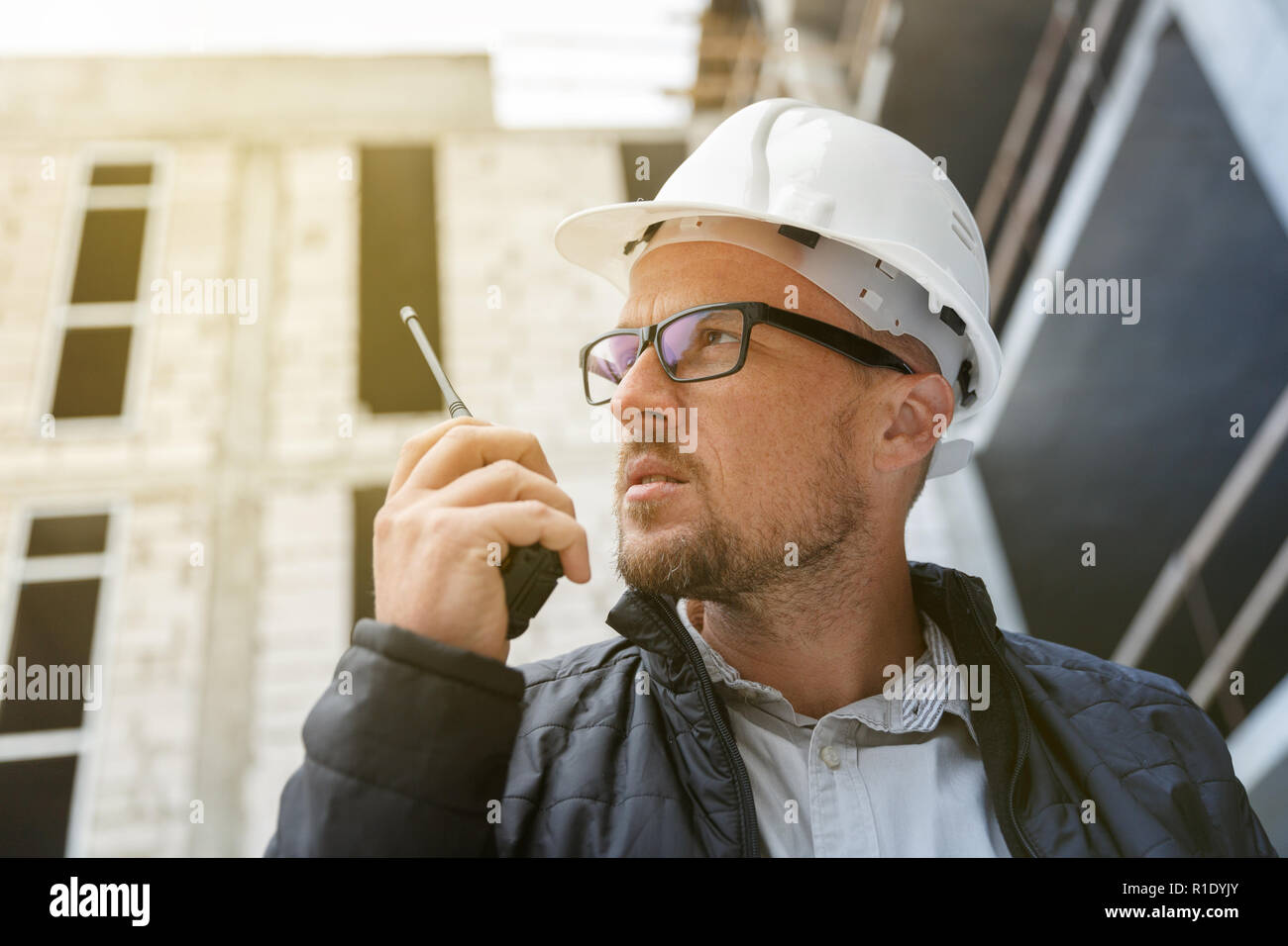 Male head engineer wearing white safety hardhat using walkie talkie ...