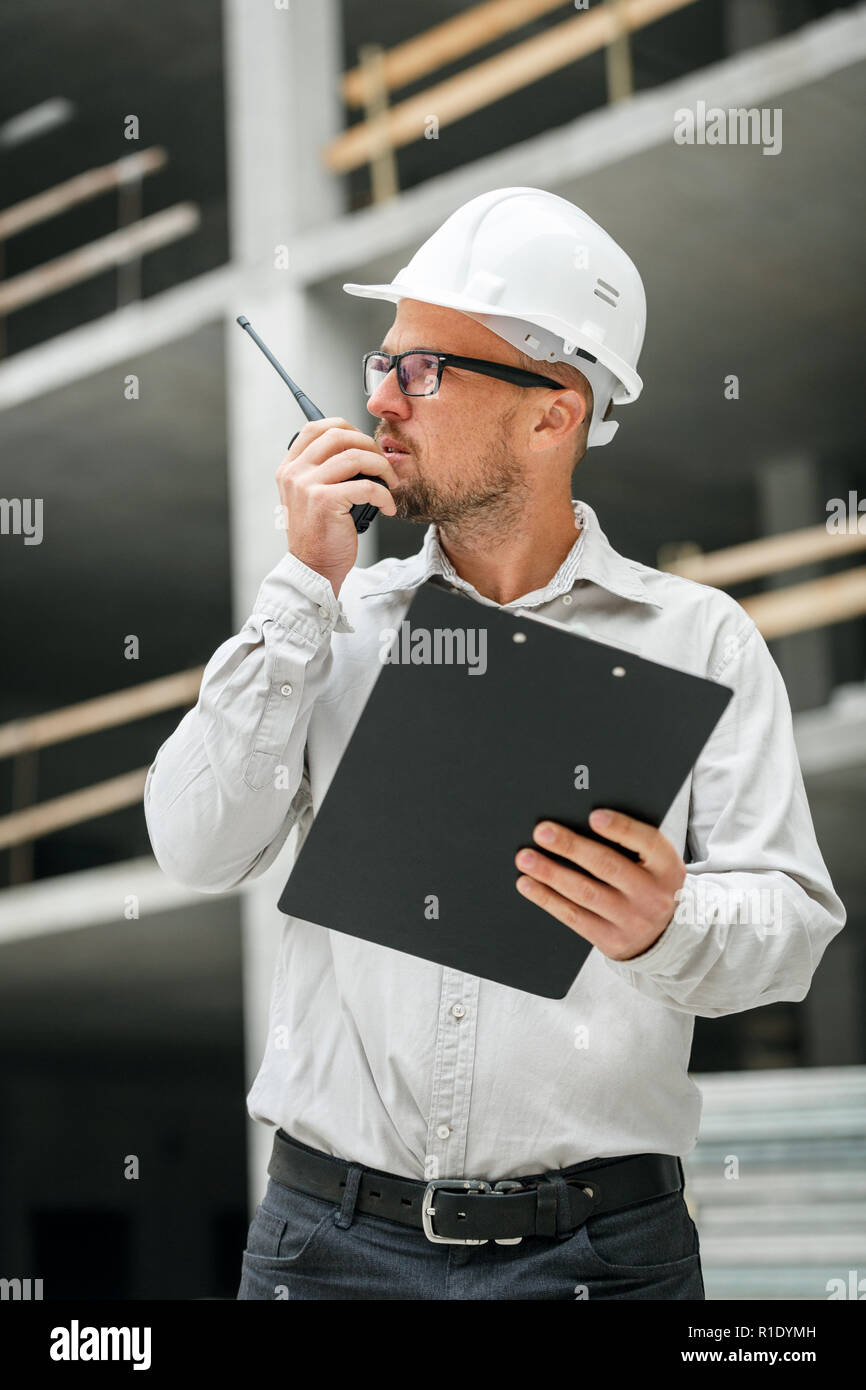 Male head engineer wearing white safety hardhat with walkie talkie and ...