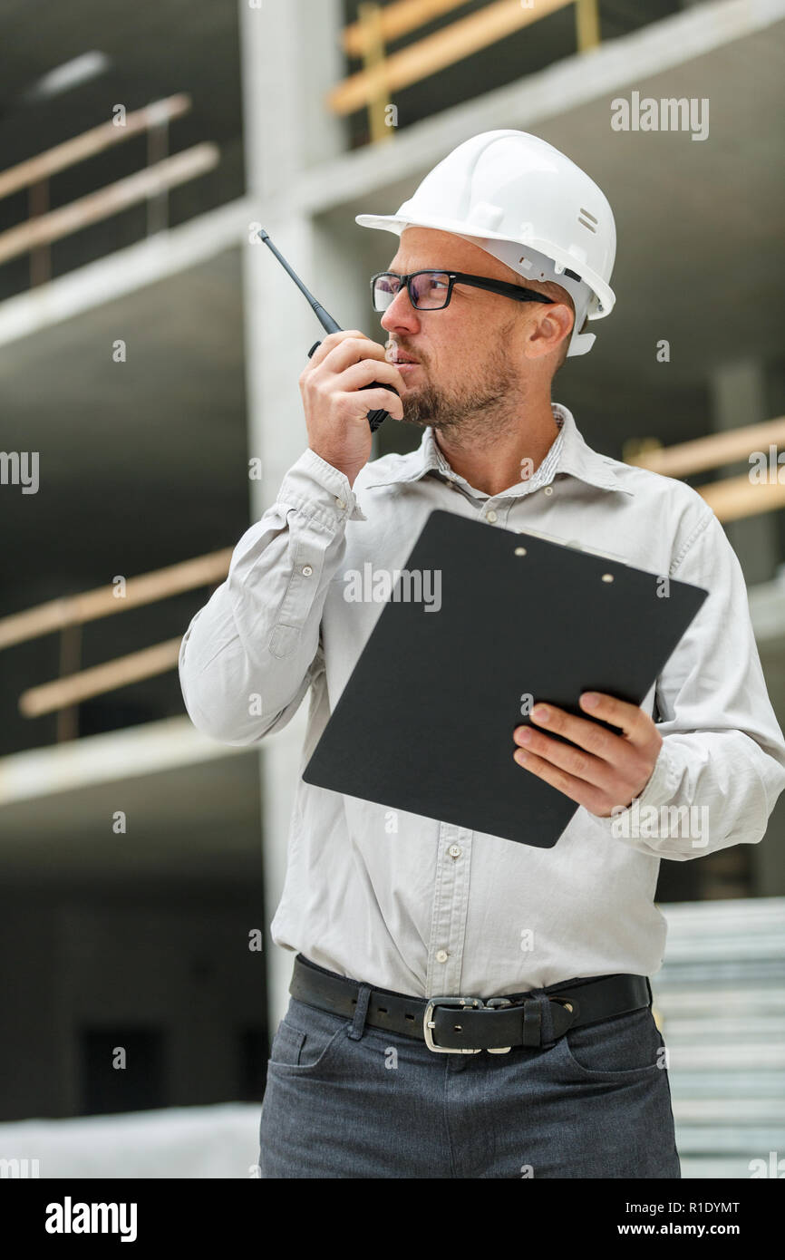 Male head engineer wearing white safety hardhat with walkie talkie and ...