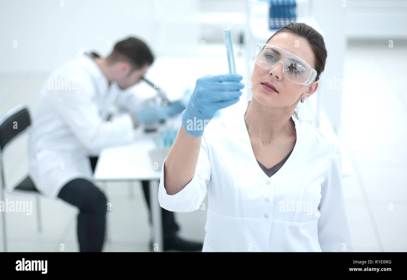 serious female scientist looks at the tube with the results of the ...
