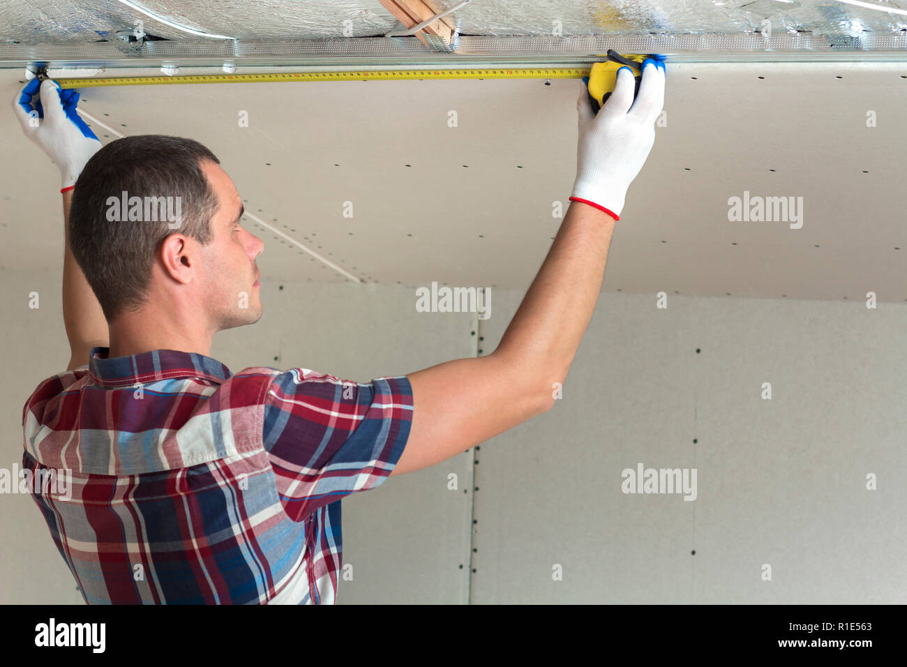 Young handsome man in casual clothing takes measurement of drywall ...