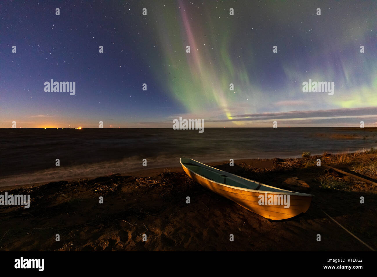 Northern lights and moonlight illuminates the rowing boat on beach ...