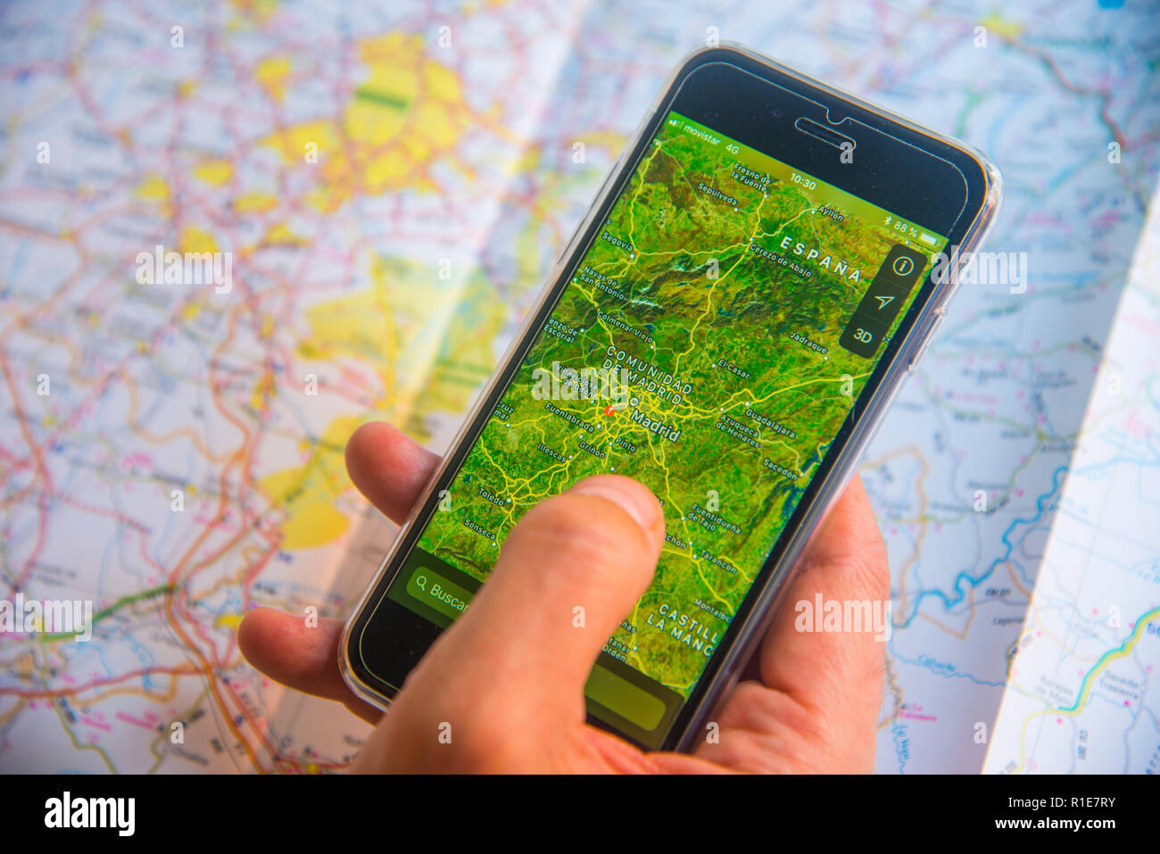 Man's hand using smartphone showing a map against a road map. Close ...