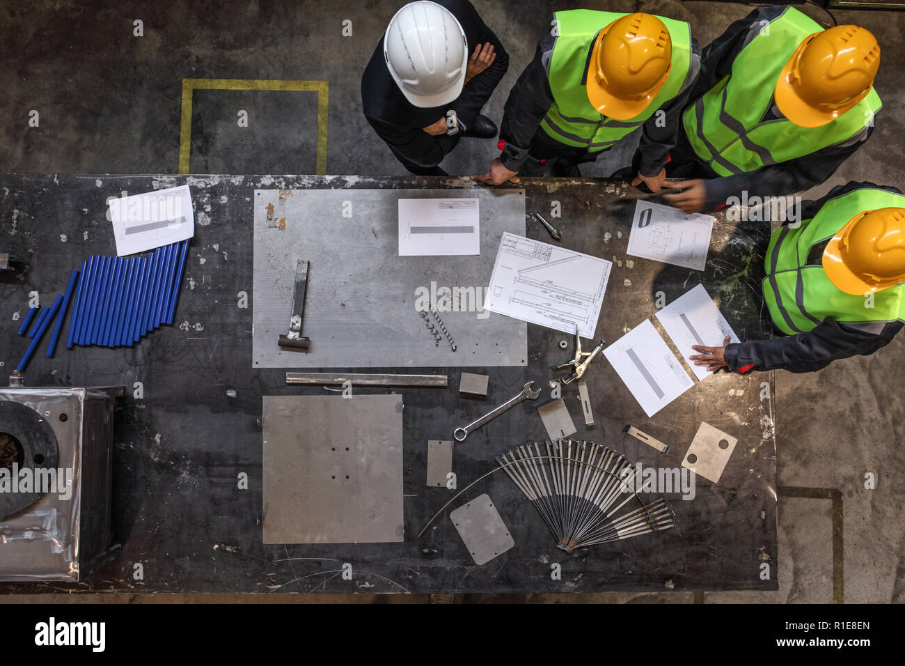 Workers and manager in safety helmets working with documents at factory ...