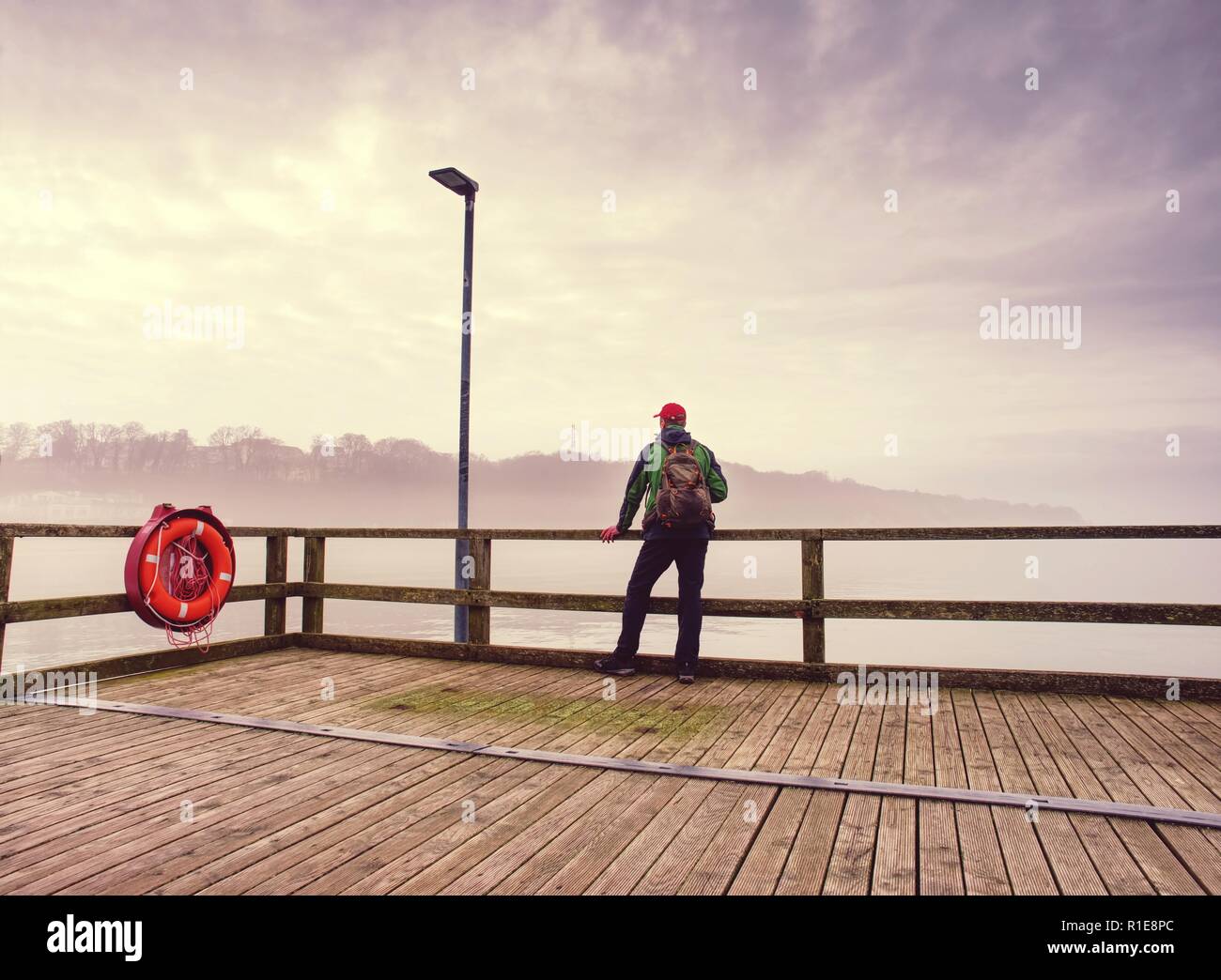 Thinking man on wooden pier on the background of sea hidden in mist ...