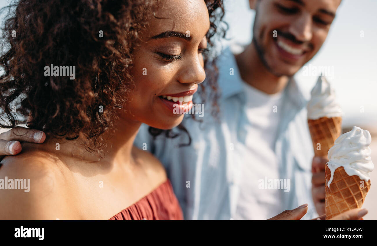 Smiling couple eating ice cream cone standing outdoors. Romantic couple ...