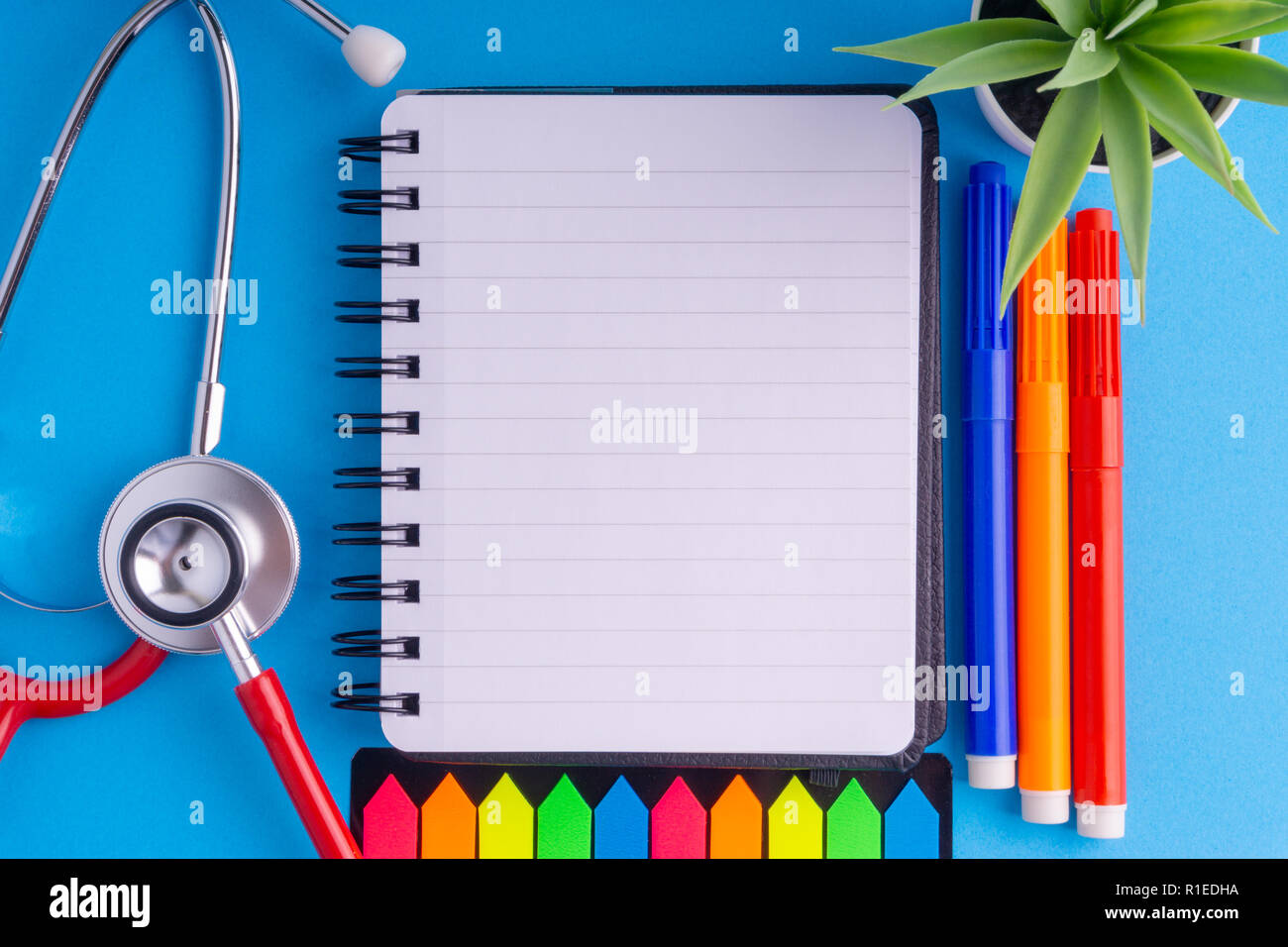 Stethoscope, sticky notes, notepad or notebook, pen and vase on blue ...