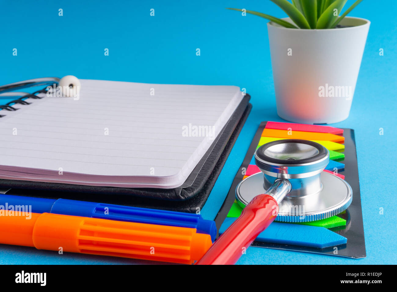 Stethoscope, sticky notes, notepad or notebook, pen and vase on blue ...