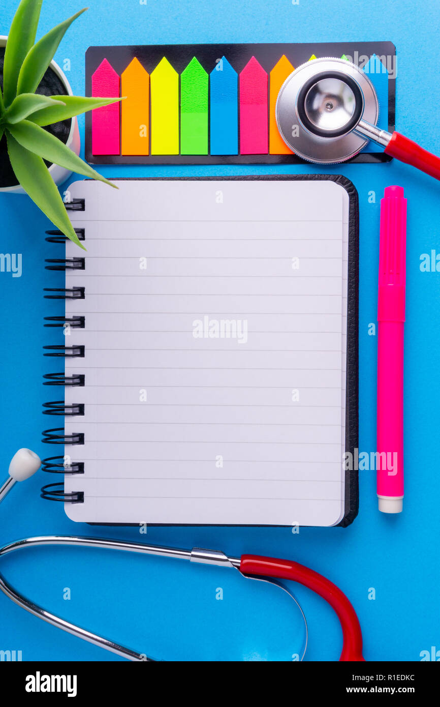Stethoscope, sticky notes, notepad or notebook, pen and vase on blue ...