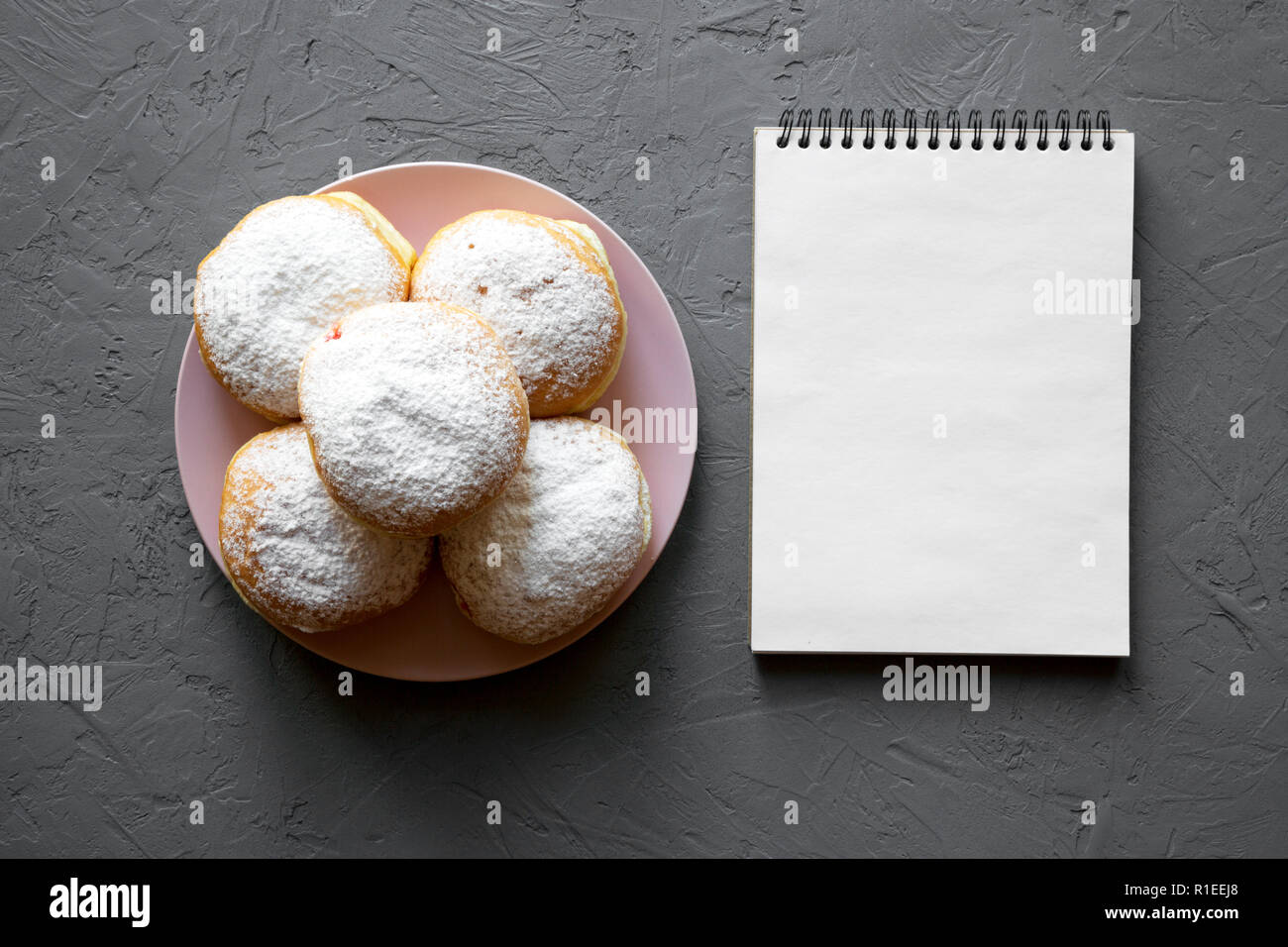 Homemade sweet donuts with powdered sugar and blank notepad on concrete ...