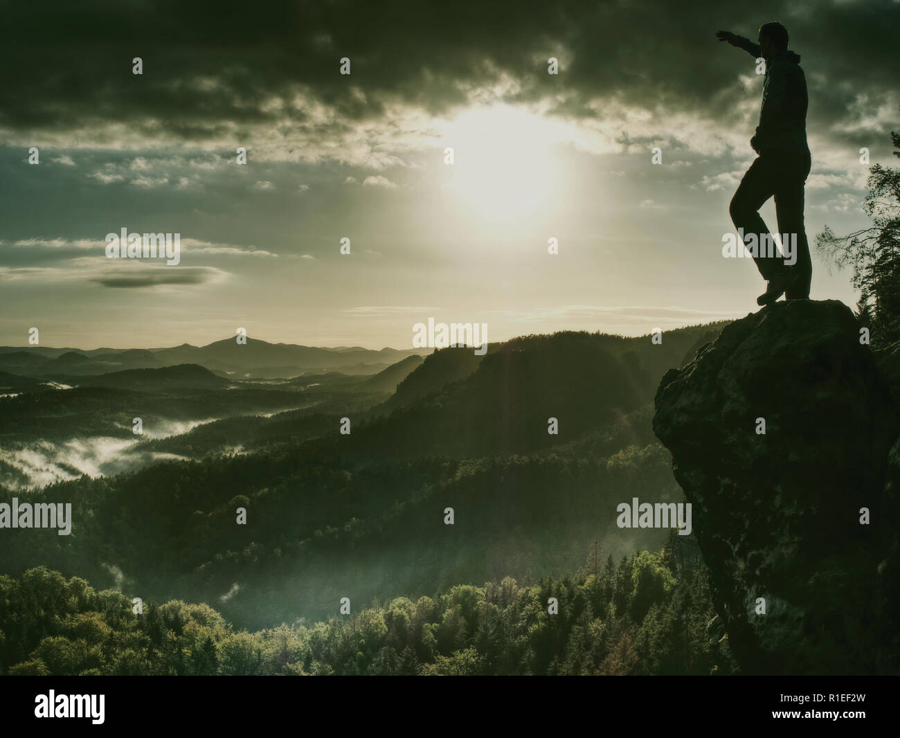 Sharp cliff edge with man watching over misty and foggy morning valley ...