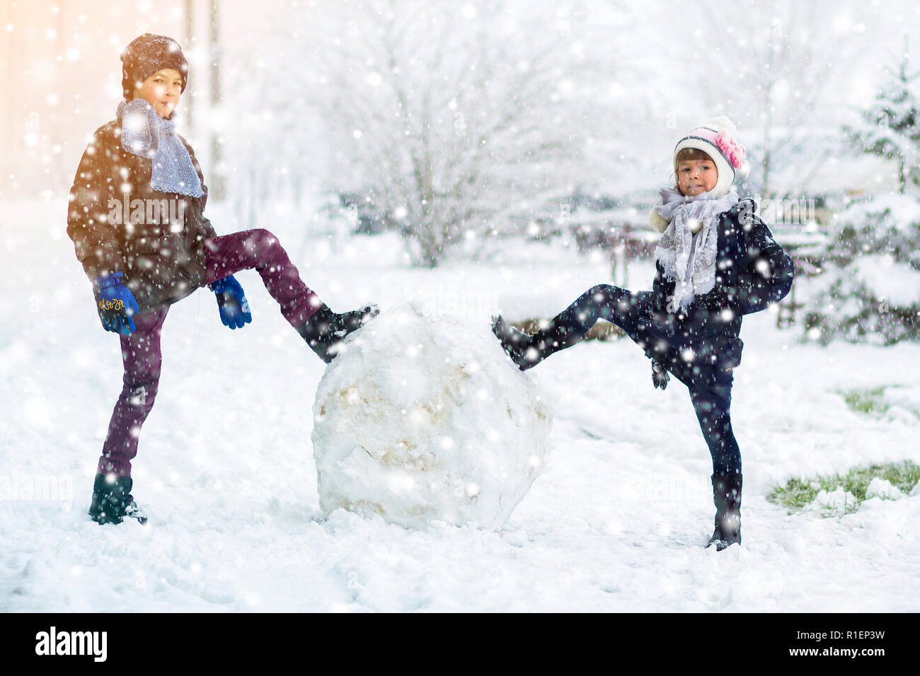 Children boy and girl outdoors in snowy winter are making a big snowman ...