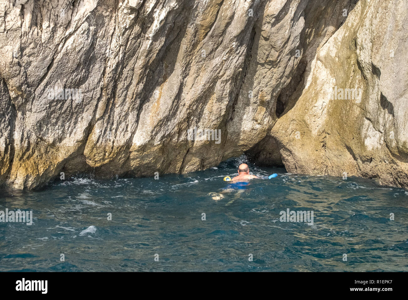 Man swims towards cave in the cliffs on the island of Capri in the Bay ...