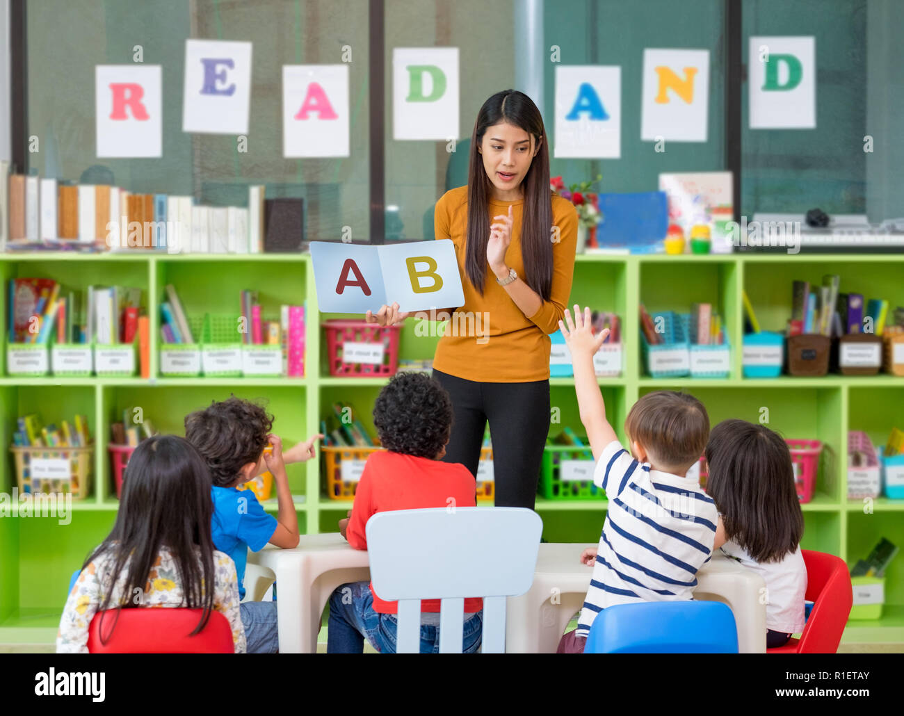 Asian female teacher teaching and asking mixed race kids hand up to ...