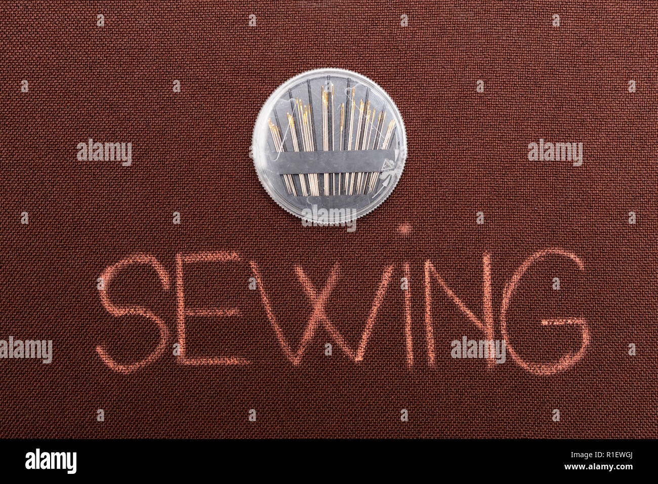 Sewing text with plastic needle holder above on brown fabric background ...