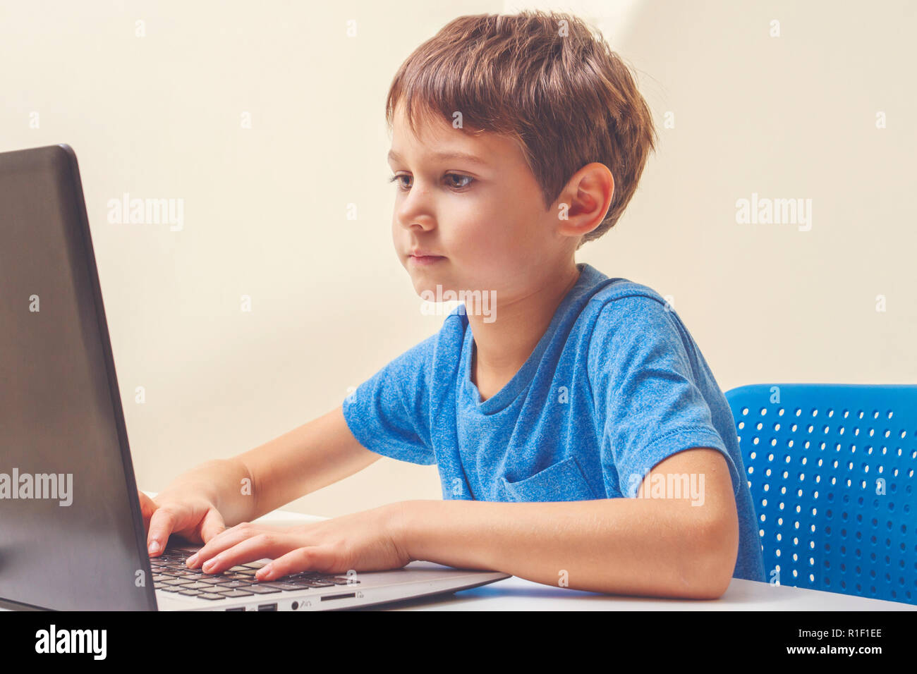 Concentrated boy sitting at desk with laptop computer and doing ...