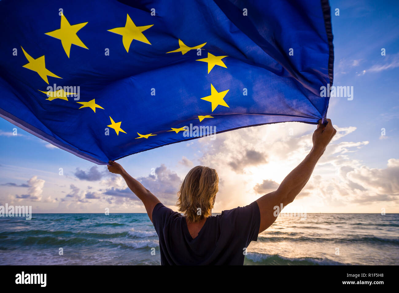 Man with blond hair holding EU European Union flag waving in the wind ...