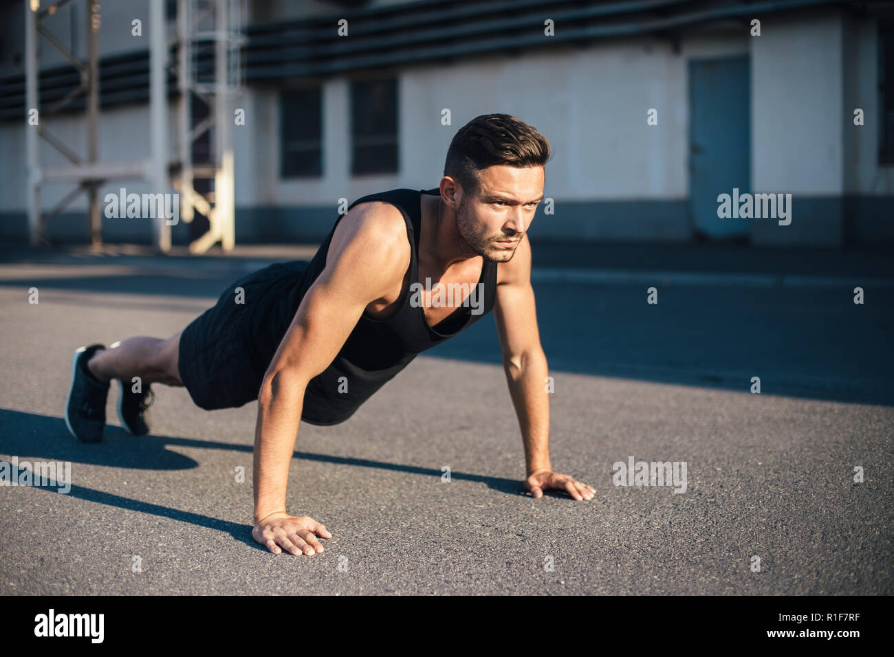 Young serious man doing pushups outdoor on industrial background ...