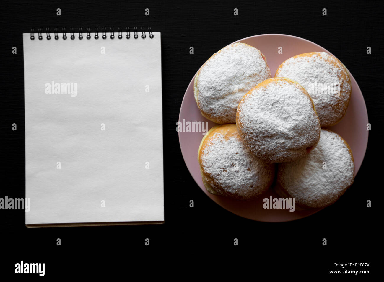 Homemade donuts with powdered sugar and blank notepad on black ...