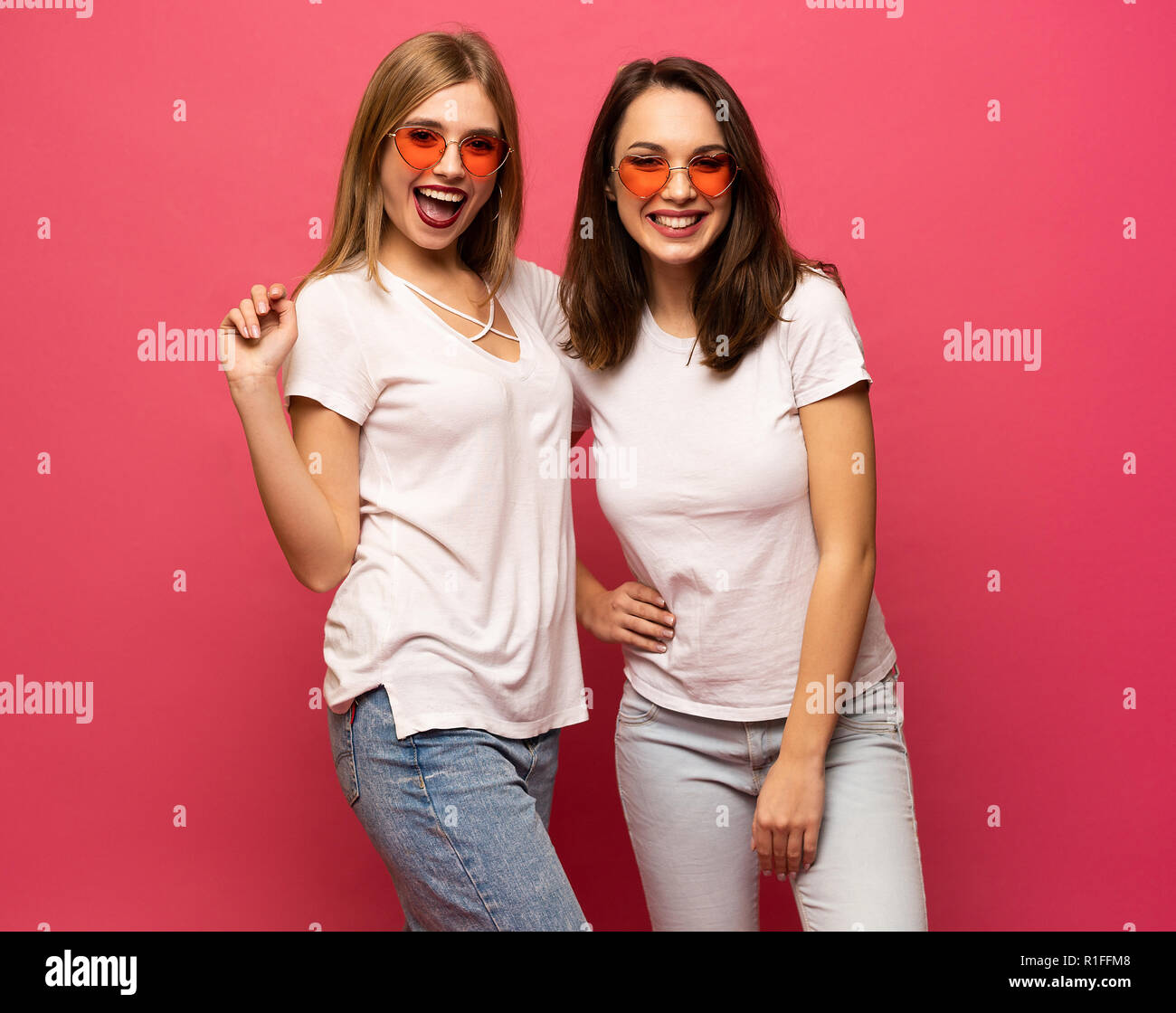 Two exited woman having fun and raising hands up. Standing on pink ...