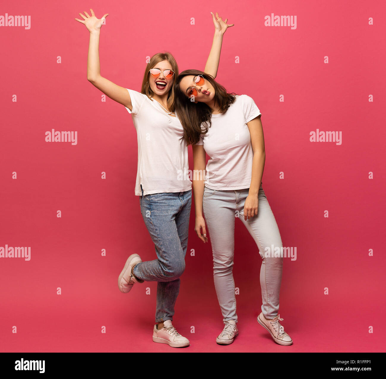 Two exited woman having fun and raising hands up. Standing on pink ...