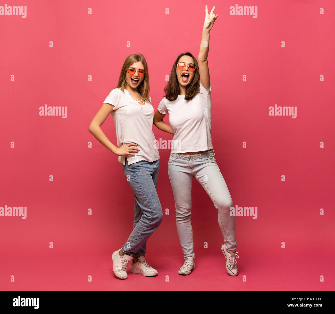 Two exited woman having fun and raising hands up. Standing on pink ...