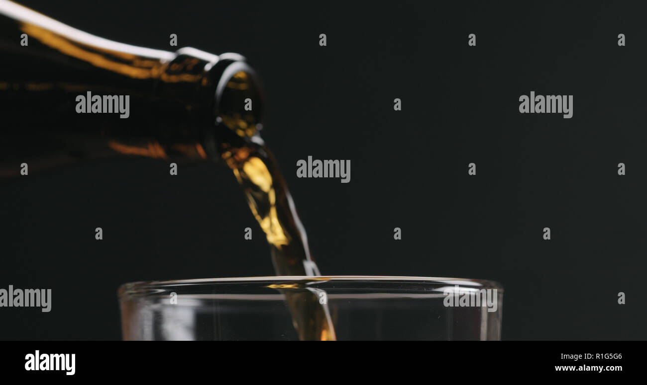 Closeup pour dark beer from brown bottle into glass on black background ...