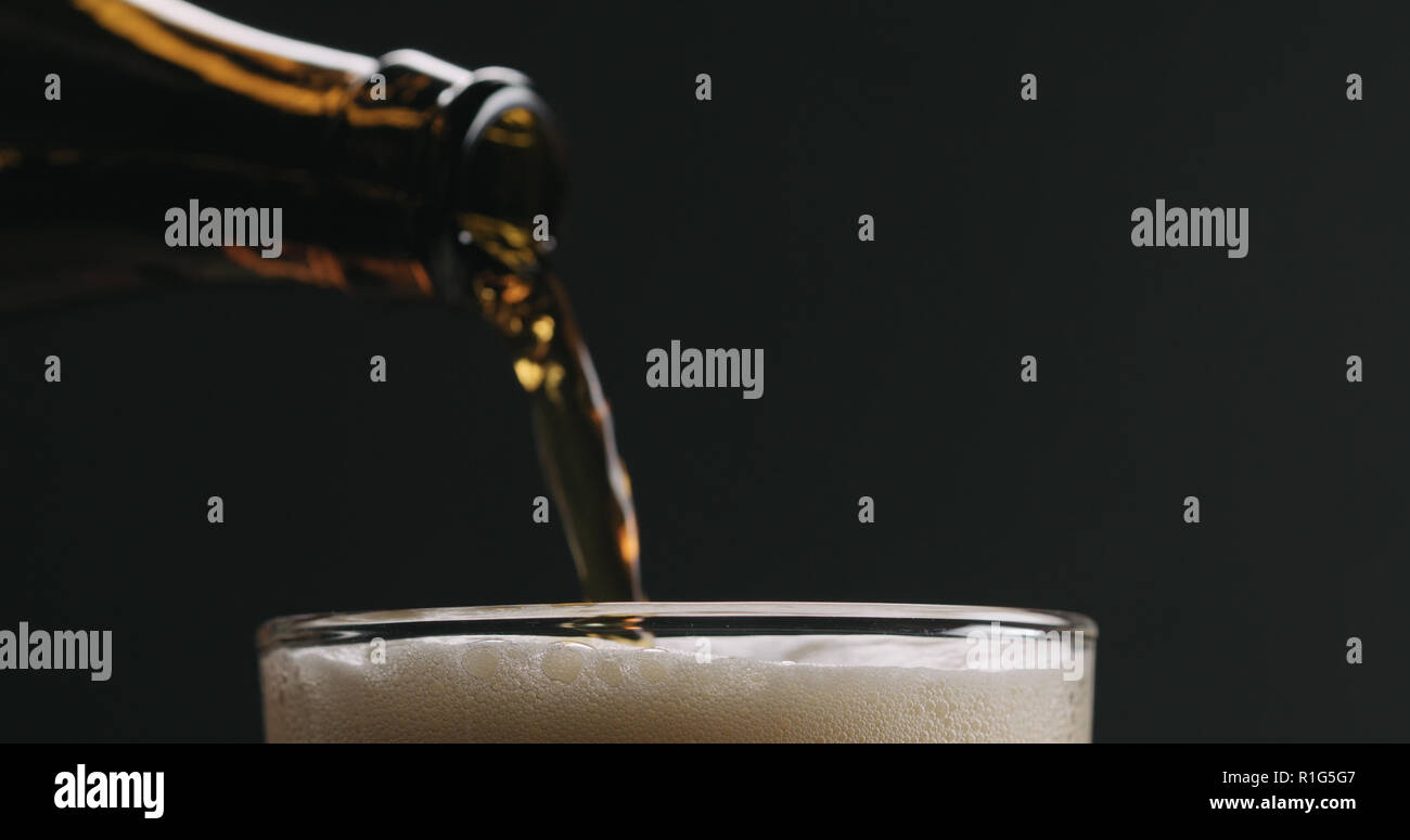 Closeup pour dark beer from brown bottle into glass on black background ...