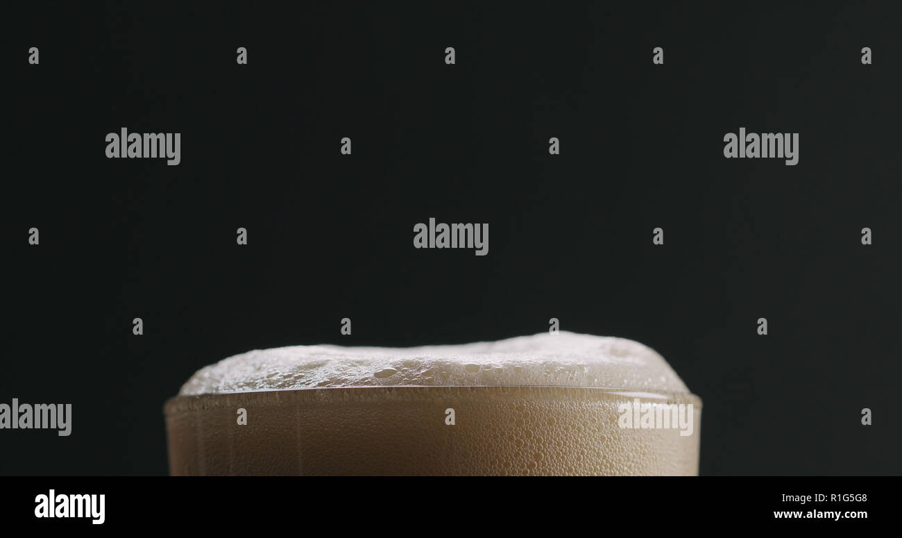 Closeup dark beer from brown bottle into glass on black background ...