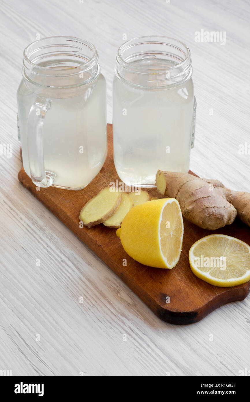 Glass jars of ginger tea with ingredients on wooden board over white ...