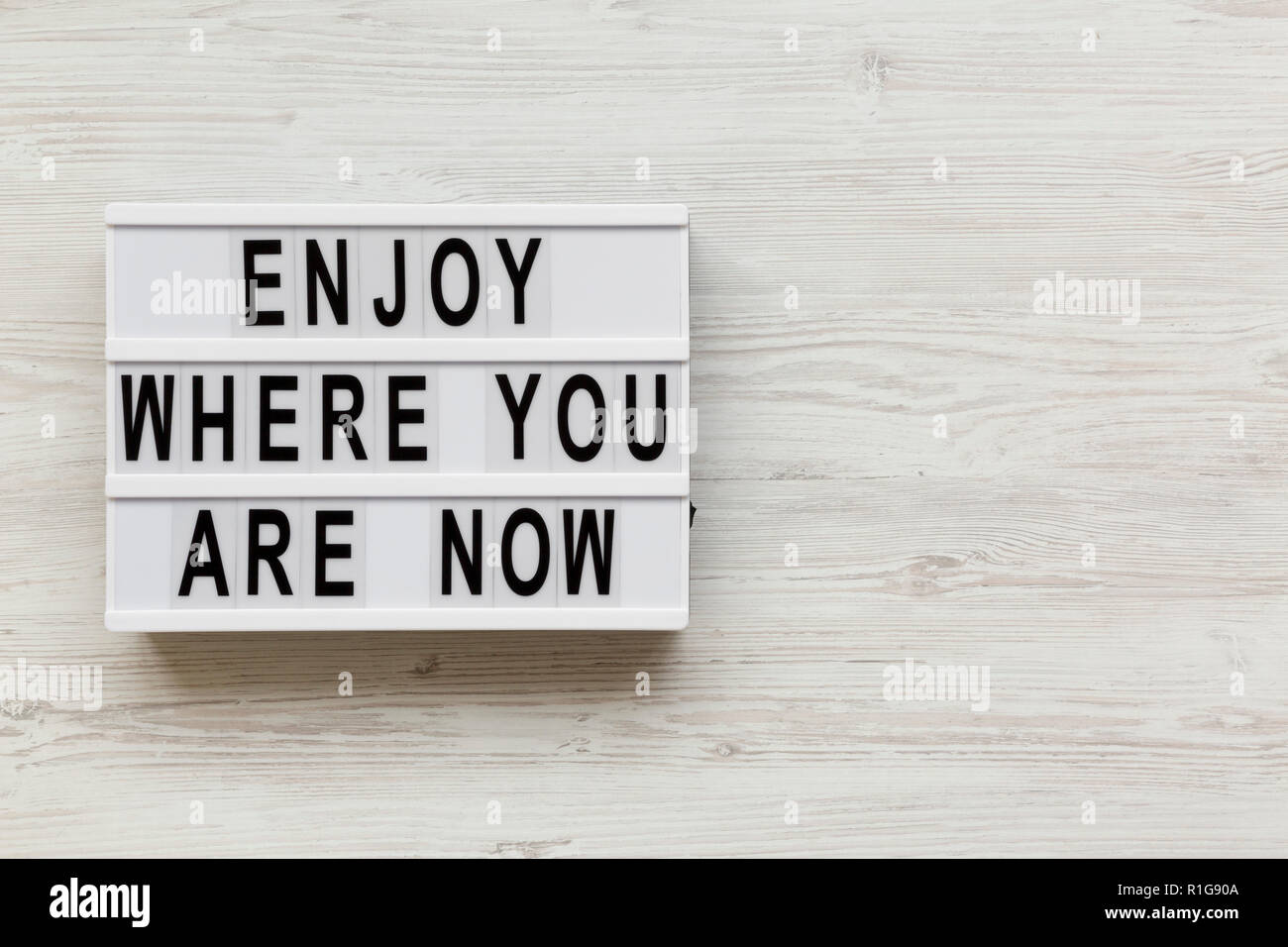 'Enjoy where you are now' words on modern board over white wooden ...