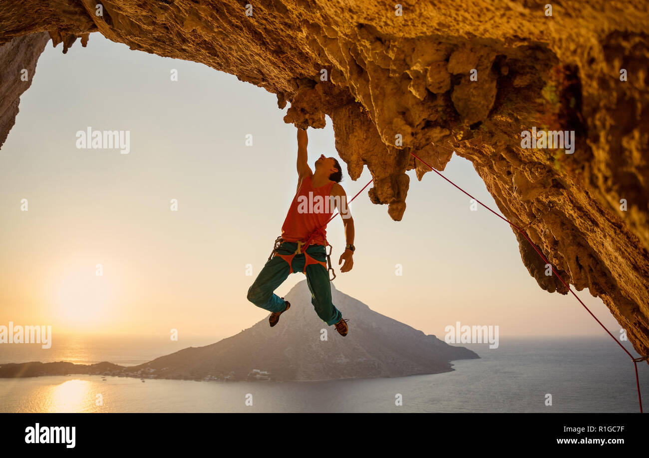 Male rock climber hanging with one hand on challenging route on cliff ...