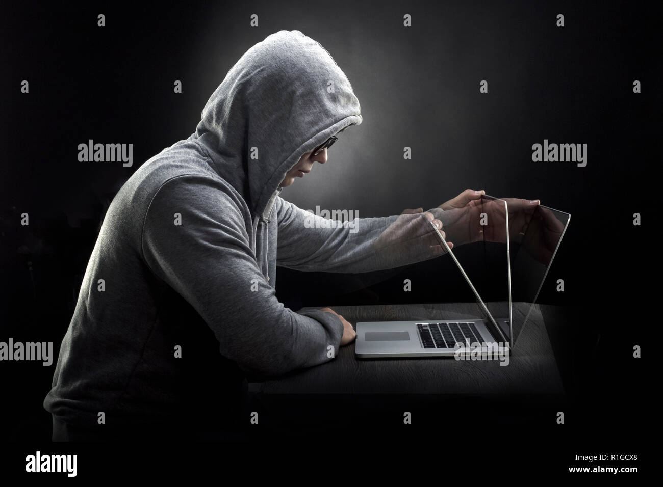 a hacker in a hood in profile sits at a laptop and starts to close it ...
