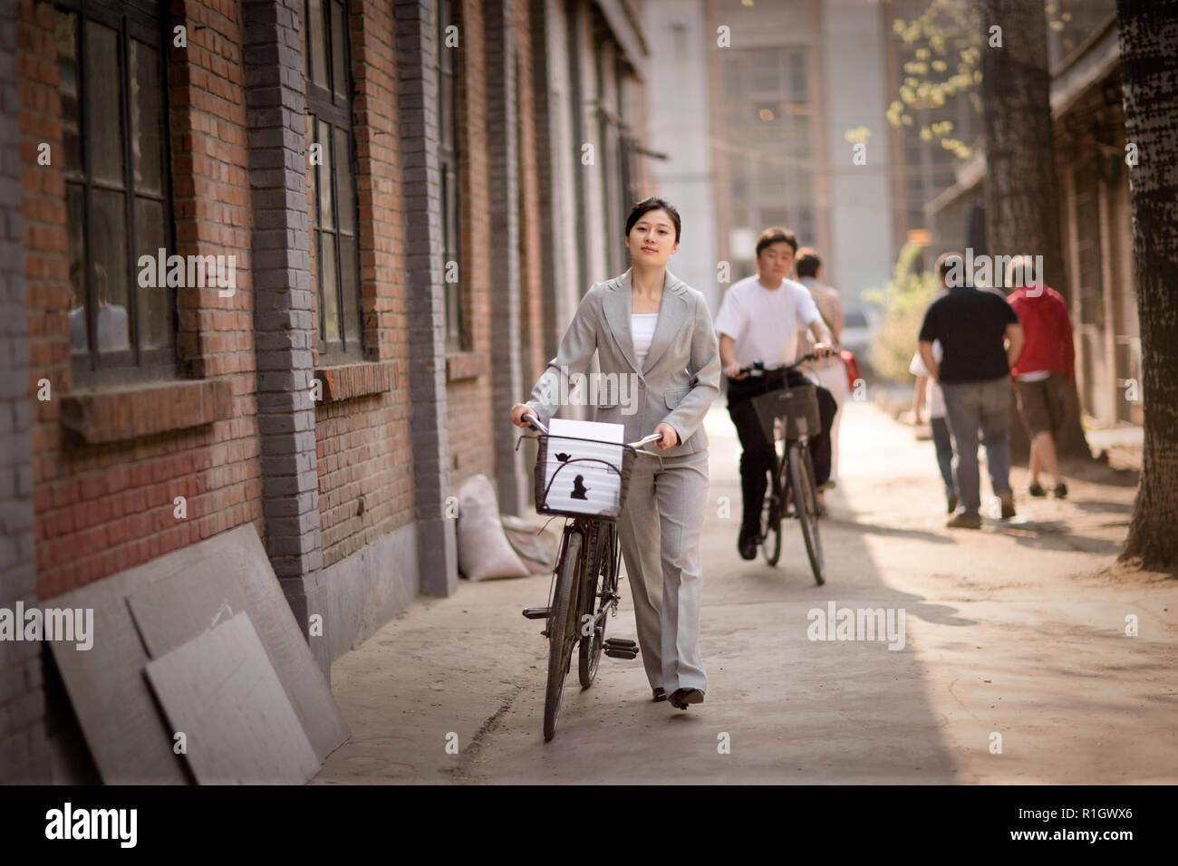 Portrait of a young adult business woman pushing a bicycle on a street ...