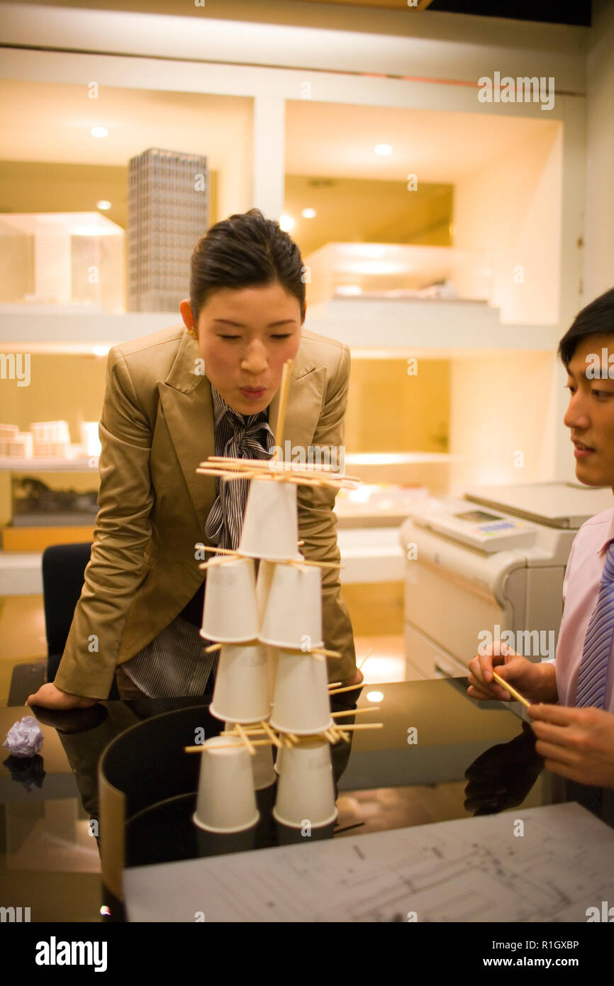 Young adult businessman and woman making a tower of cups in an office ...
