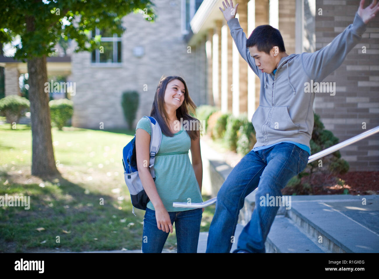 Teenage boy sliding down handrail to impress teenage girl Stock Photo ...
