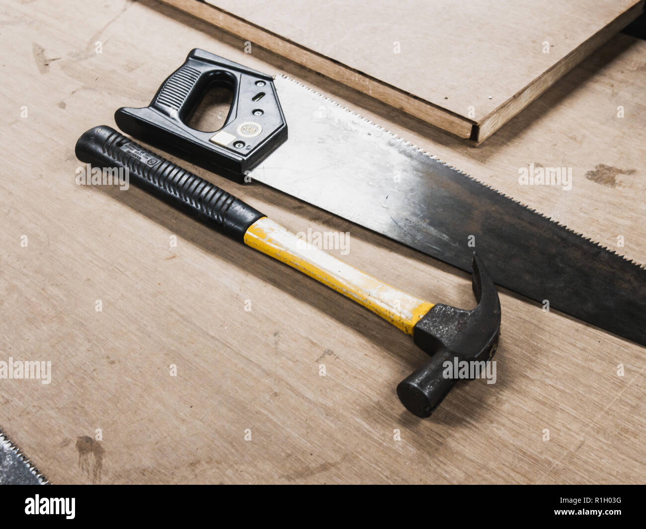 Hammer, hand saw, and wooden plank placed on a wooden table in workshop ...