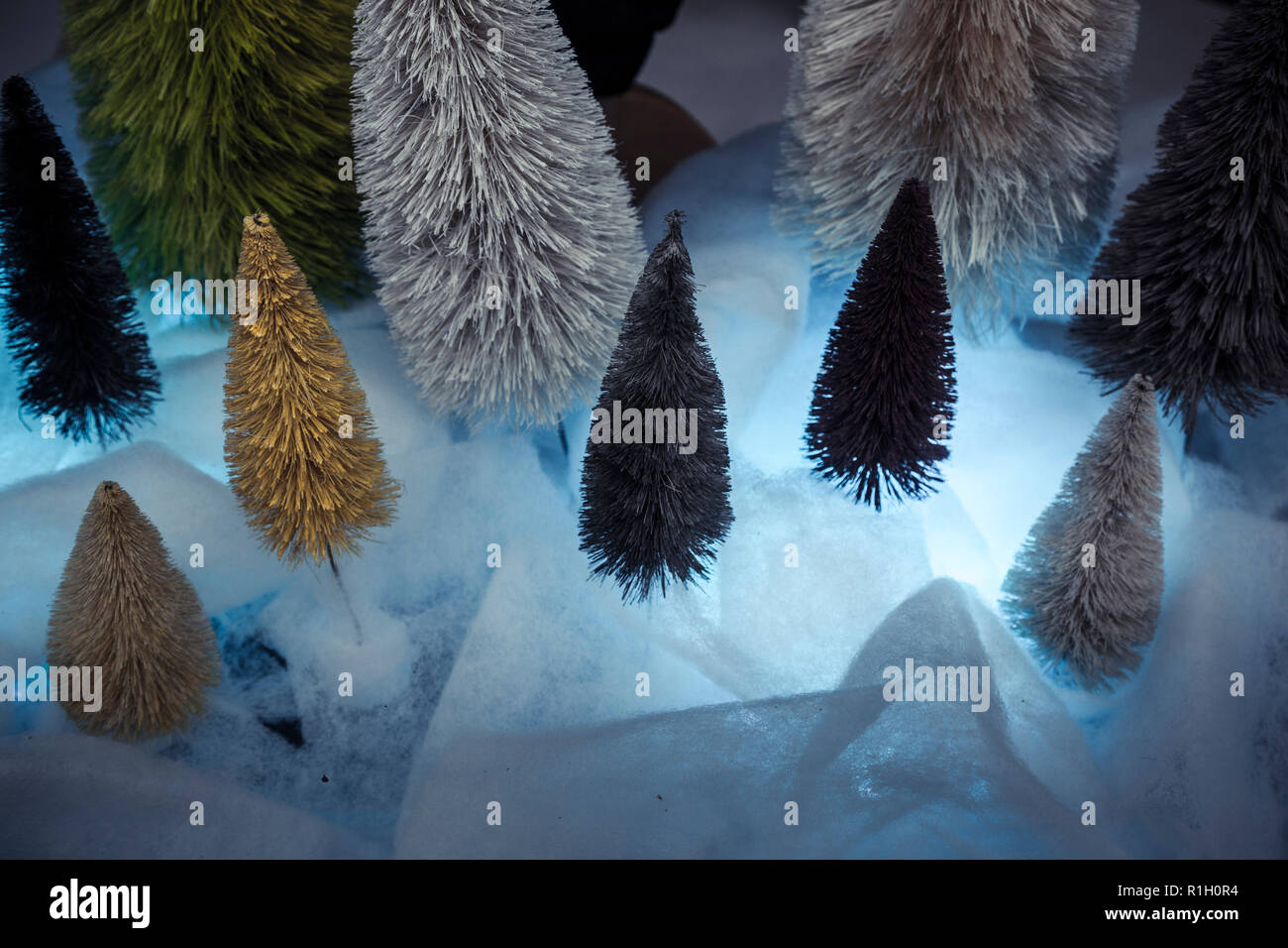Seasonal shop window display of miniature coloured fir trees and mock ...