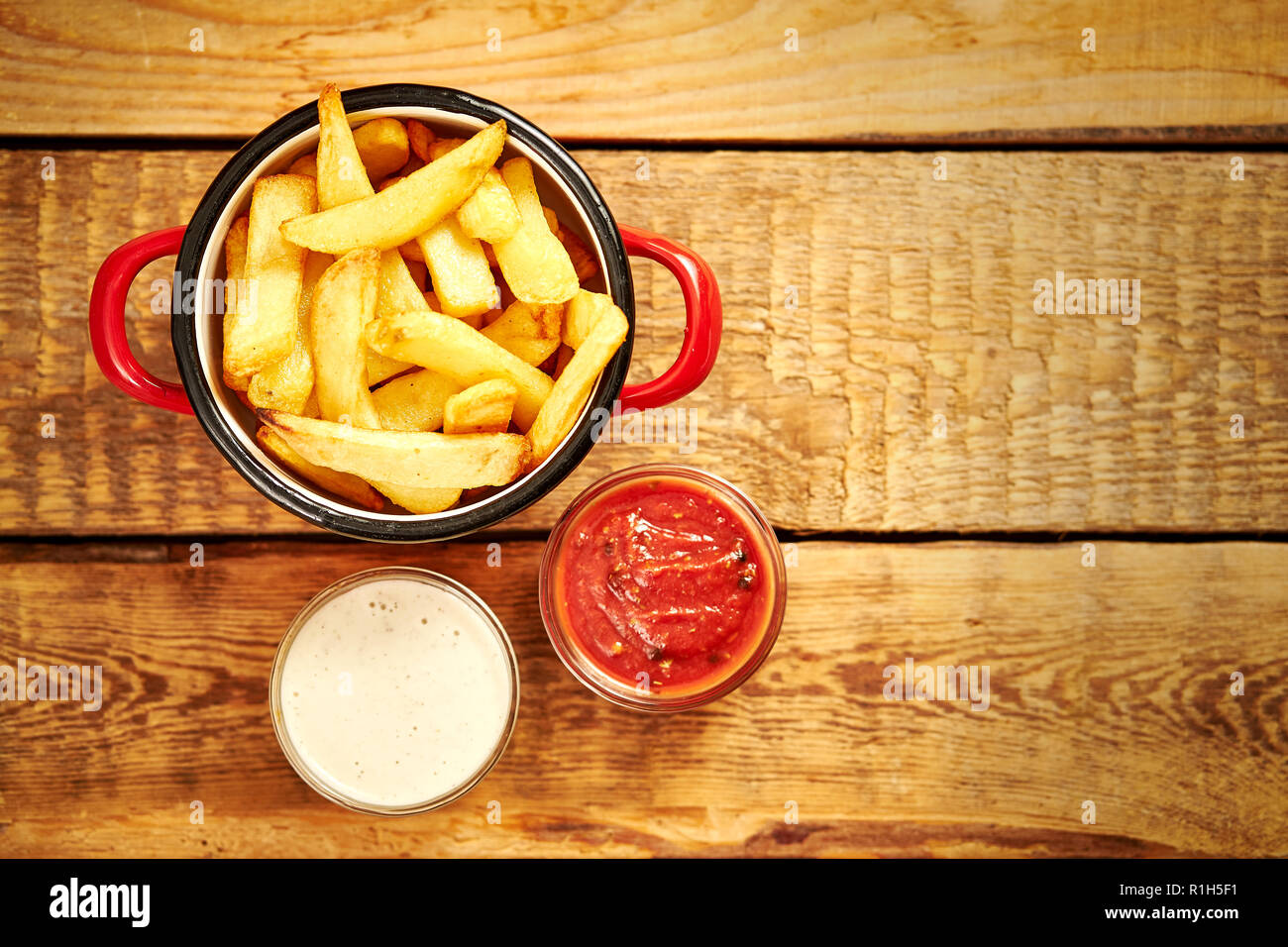 top view of delicious french fries in a red pot with sauces on an old ...